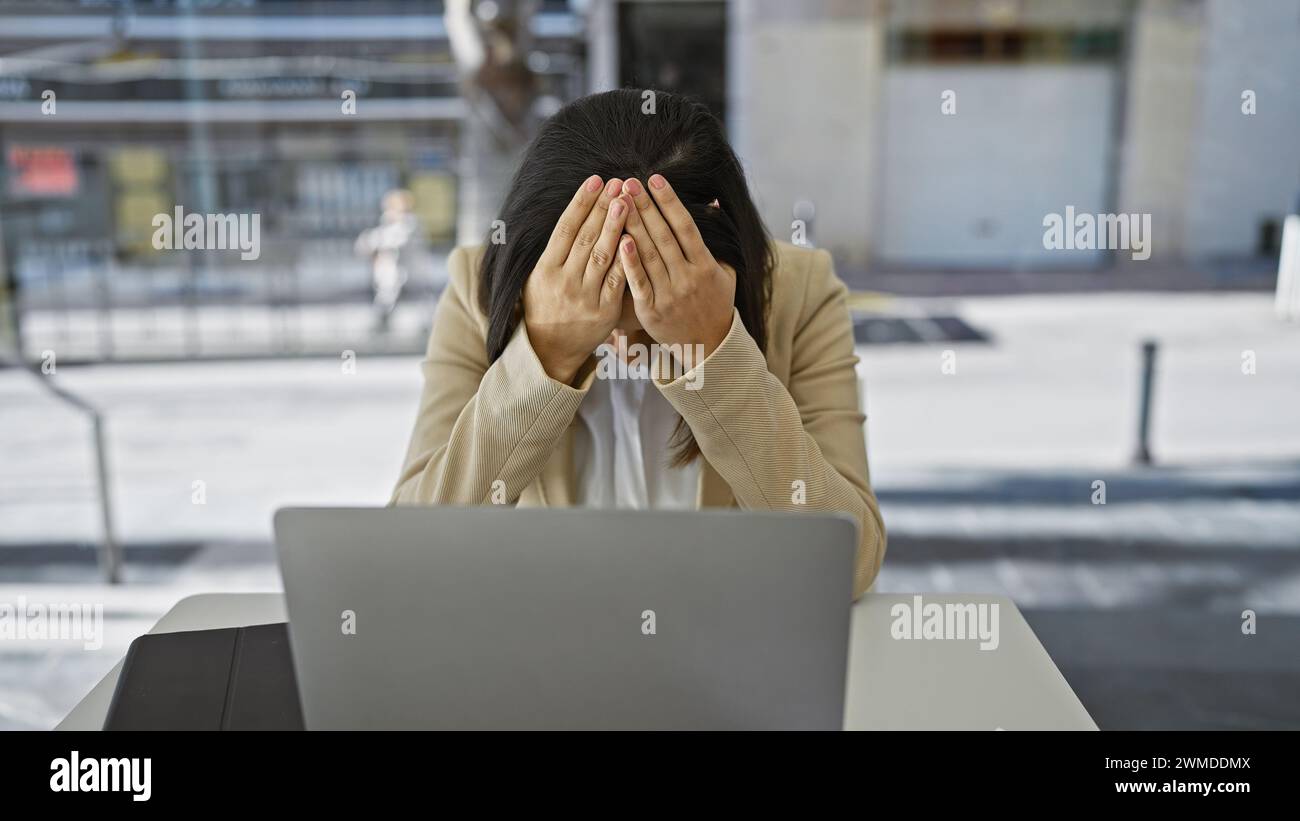 Stressed woman sitting at a computer outdoors with her head in hands ...