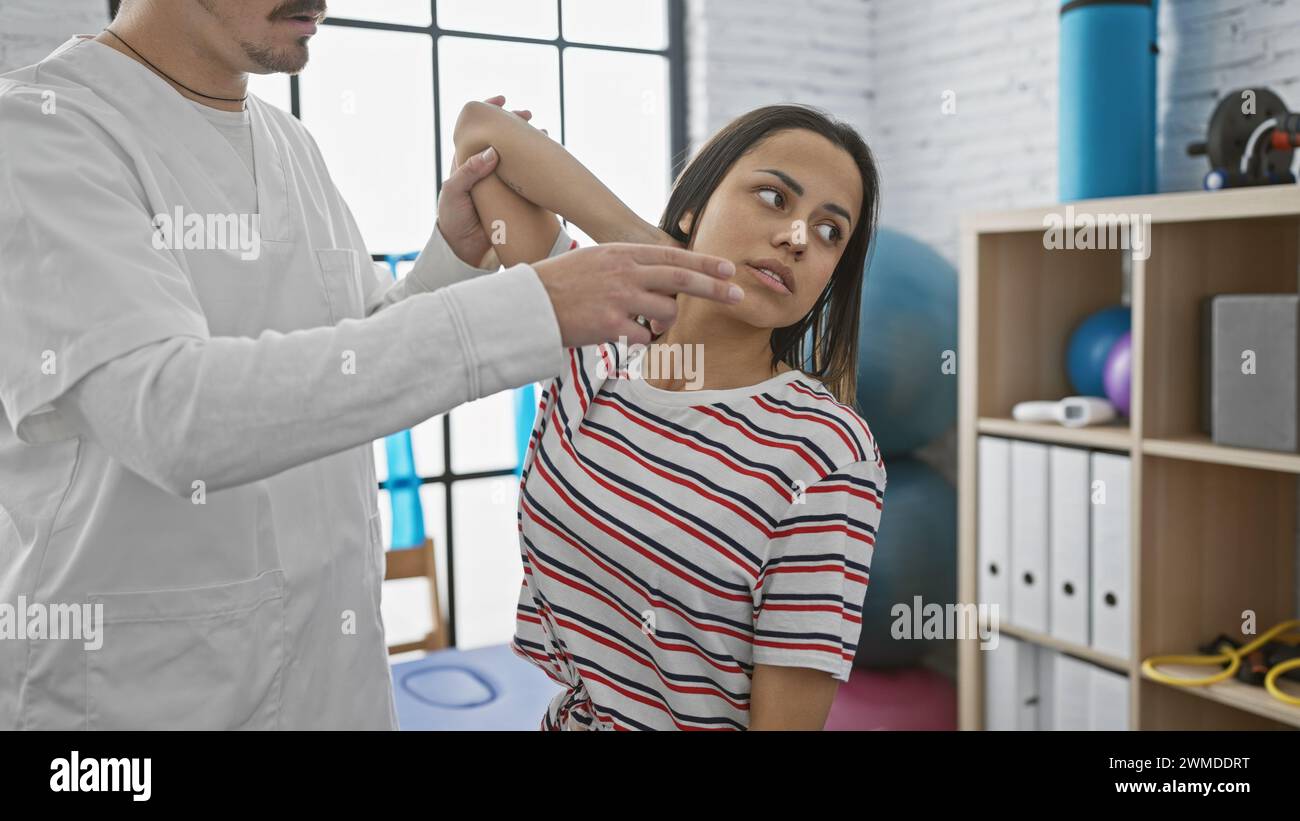 In an indoor physiotherapy clinic, a male therapist assesses the arm of ...