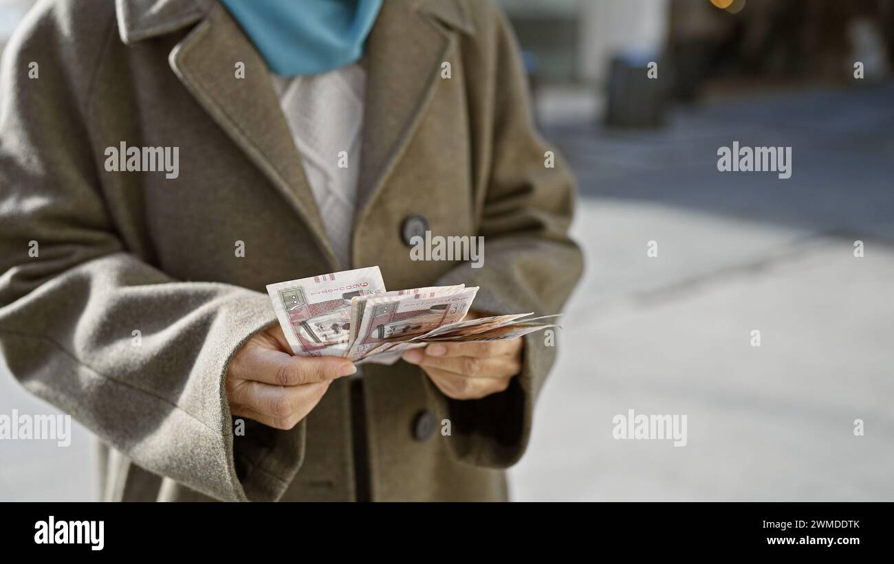 Middle-aged woman counting saudi riyal banknotes on an urban street ...