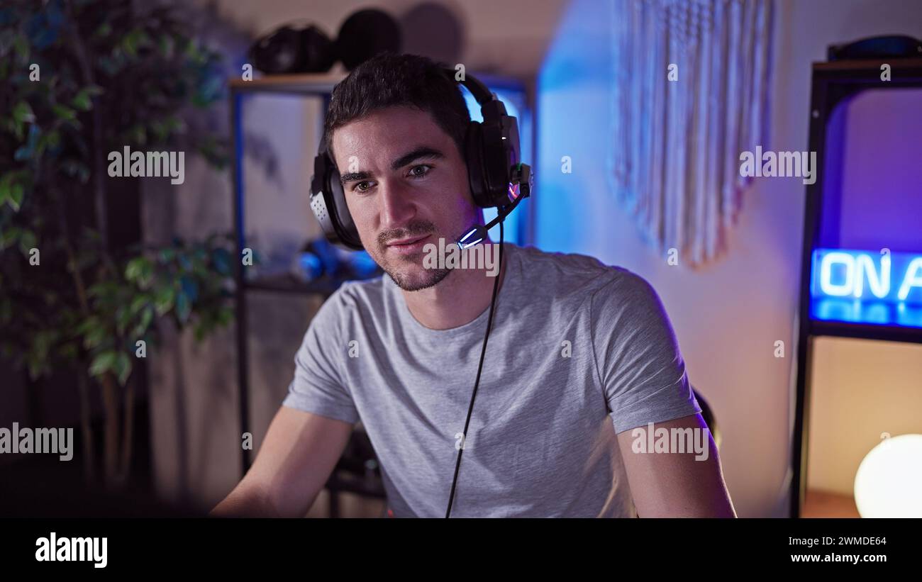 A young hispanic man wearing headphones in a dark indoor gaming room ...