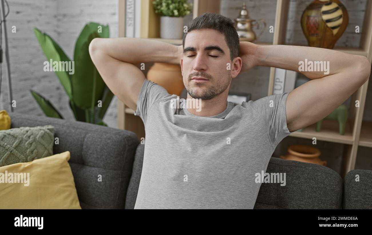 A relaxed hispanic man lounging on a grey sofa in a cozy living room ...
