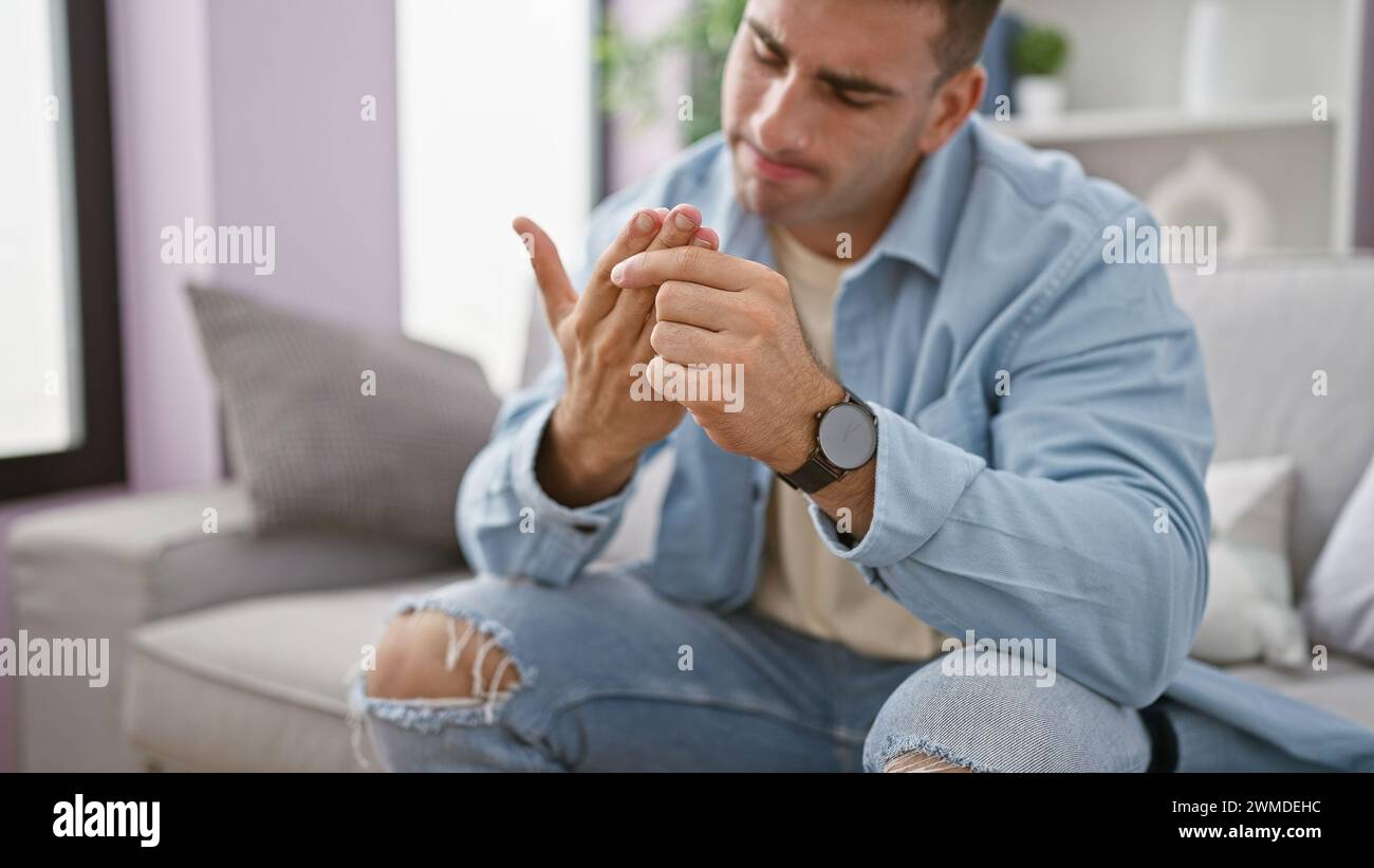 Unhappy, young hispanic man reluctantly sitting in his cozy living room ...
