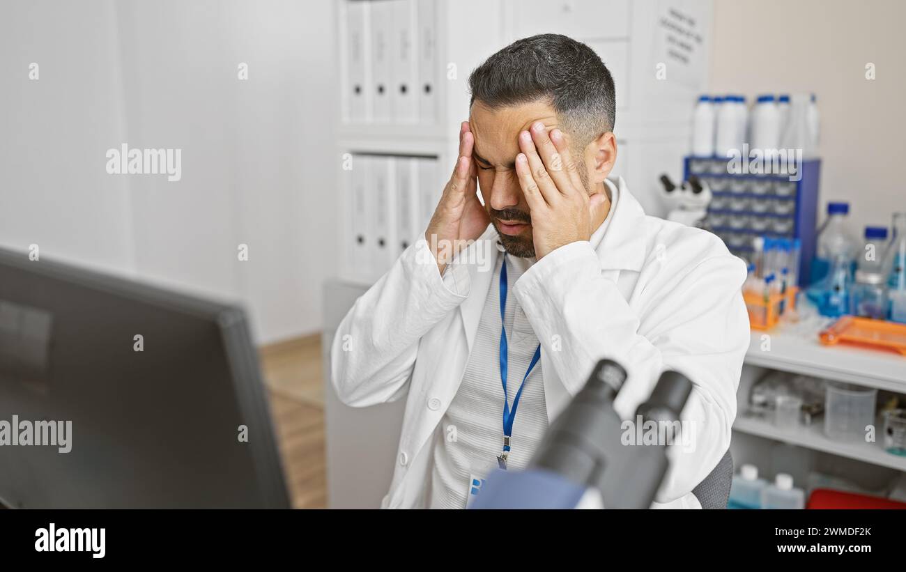Stressed hispanic man in lab coat feeling headache at medical center ...