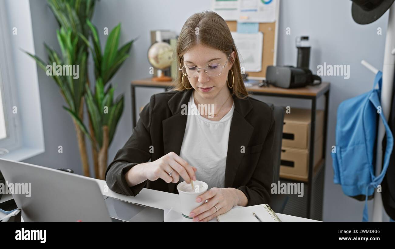 A young professional woman stirs coffee in a modern office, portraying ...