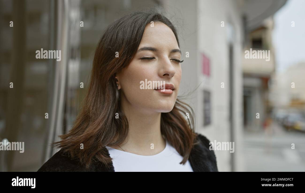 A calm hispanic woman with a subtle smile stands outdoors on a city ...