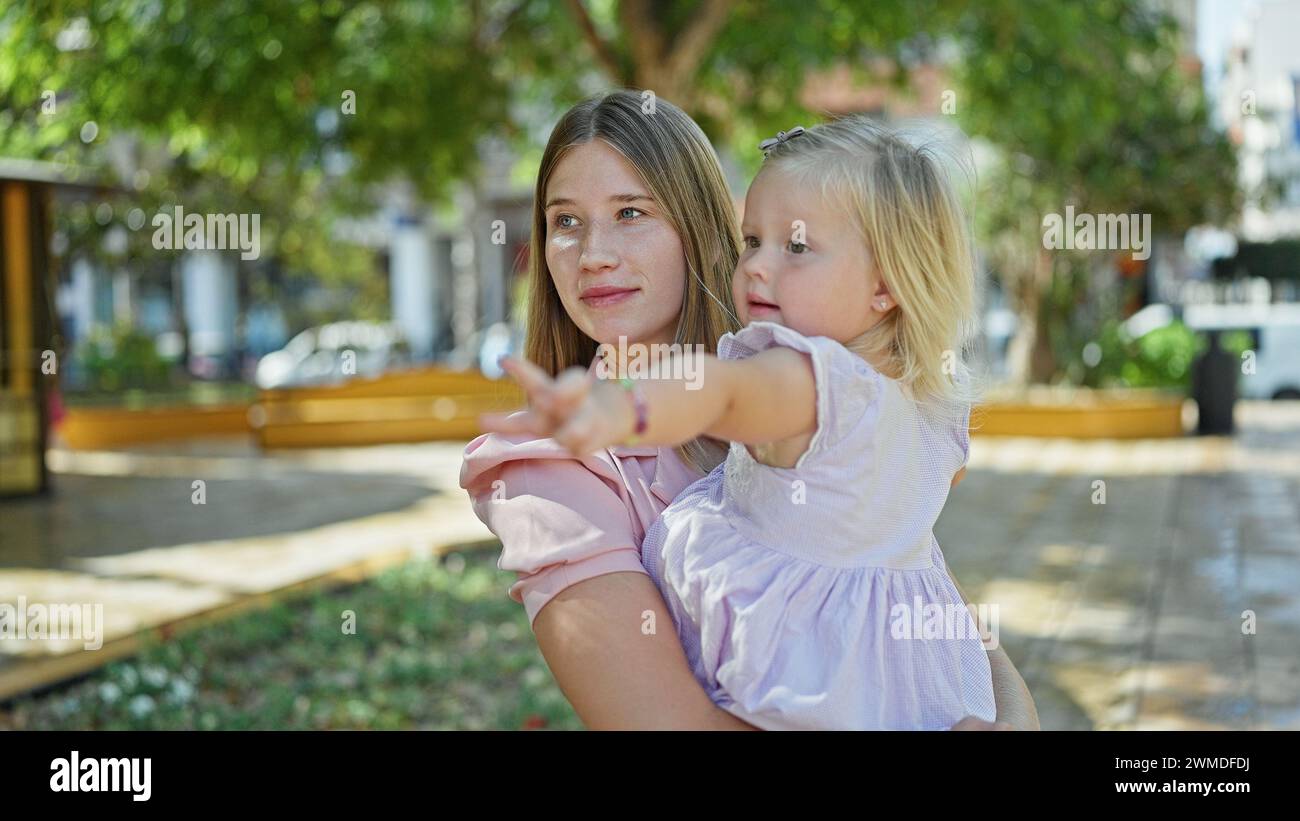 Caucasian mother, pointing to the side, holding daughter in arms while ...