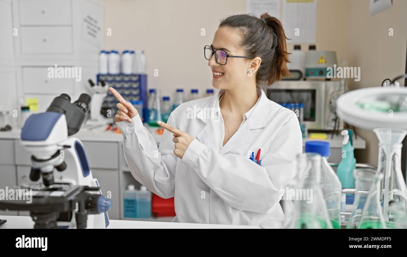 Smiling young woman scientist in laboratory pointing at chemical ...