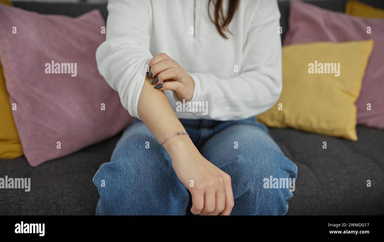 A young woman scratches her arm while sitting comfortably in a modern ...