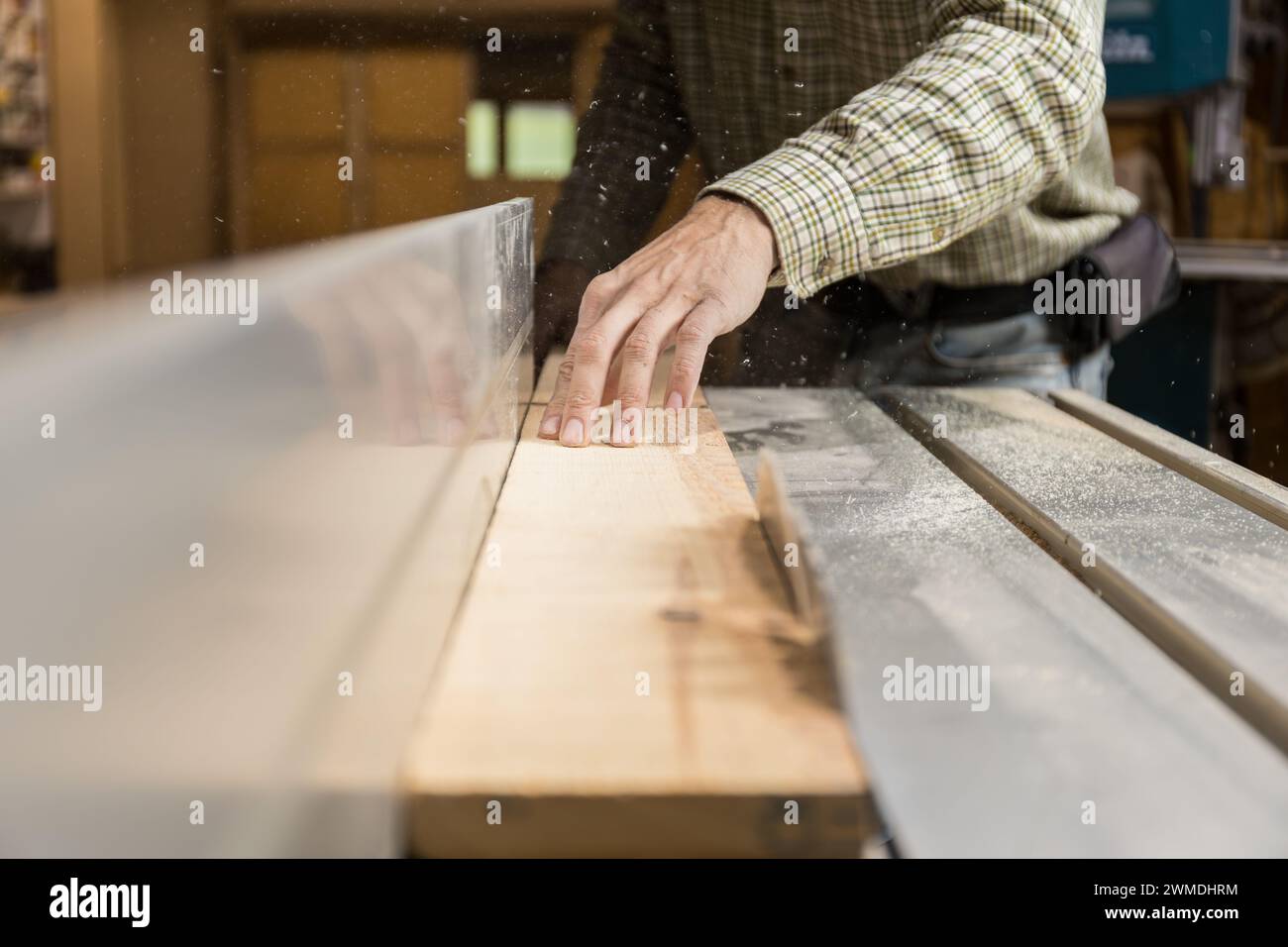 Horizontal photo an artisan's steady hands push a piece of lumber past ...