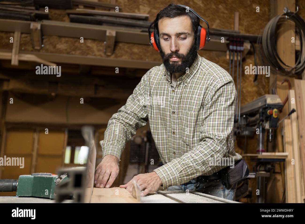 Horizontal photo serious carpenter with hearing protection operates a ...