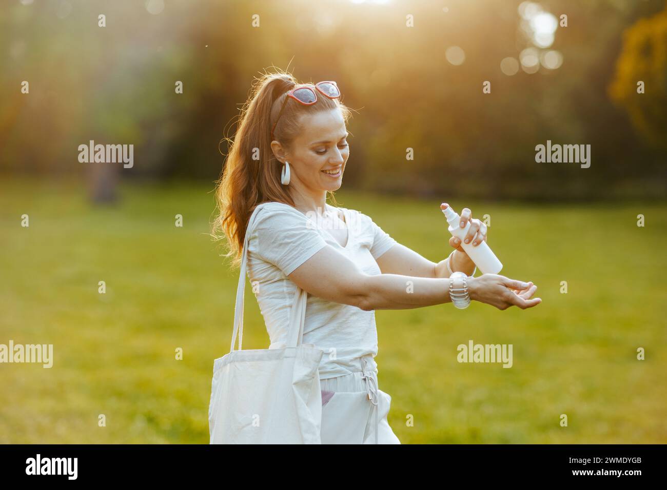 Summer time. happy trendy woman in white shirt with tote bag using spf ...