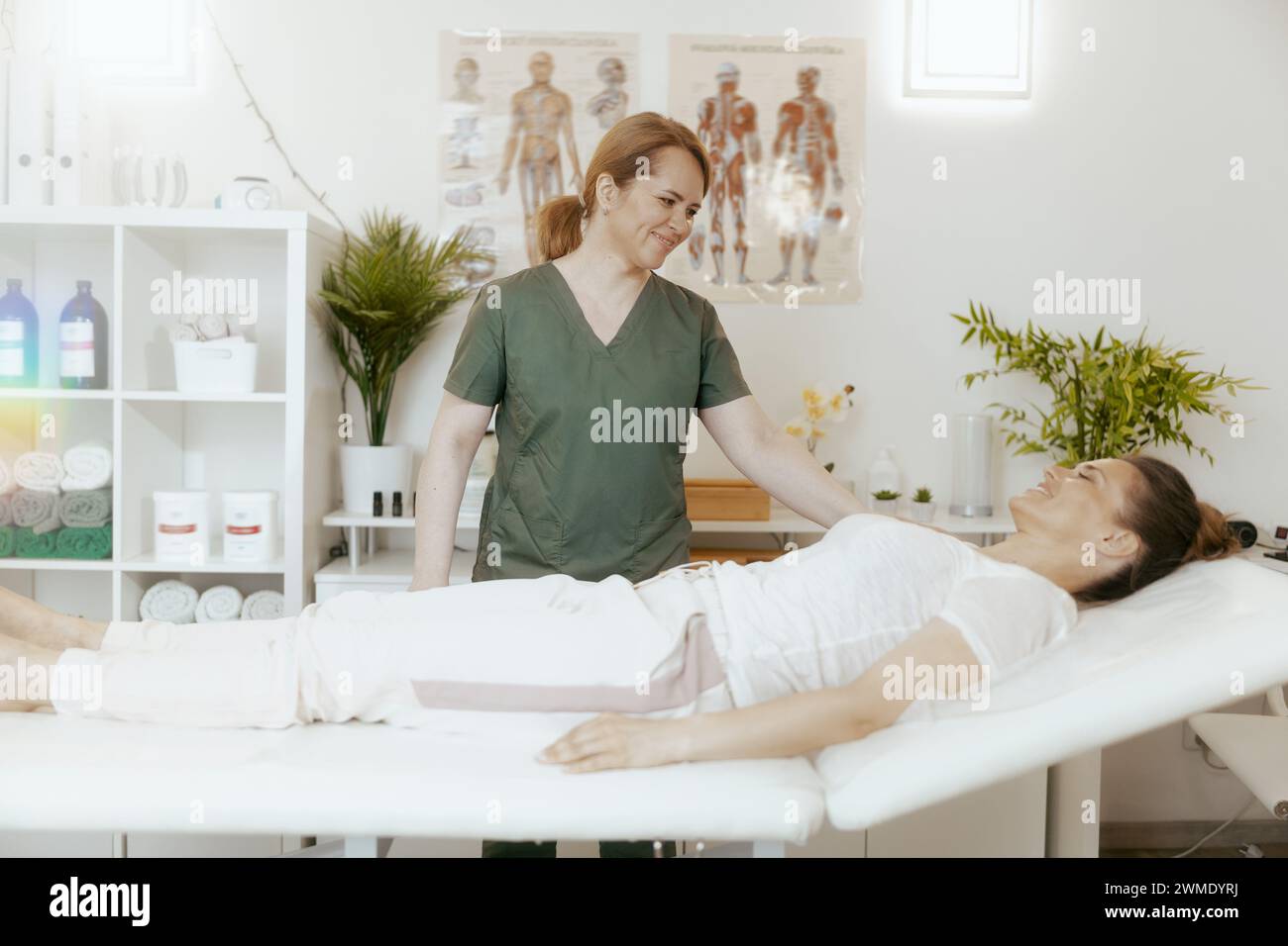 Healthcare time. smiling massage therapist woman in massage cabinet with client doing checkup ...