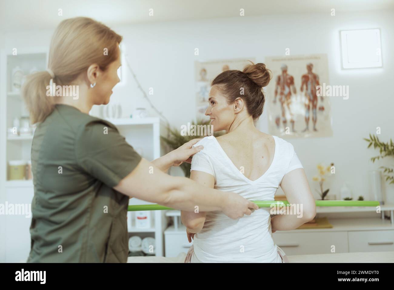Healthcare time. smiling female massage therapist in massage cabinet with client conducting ...