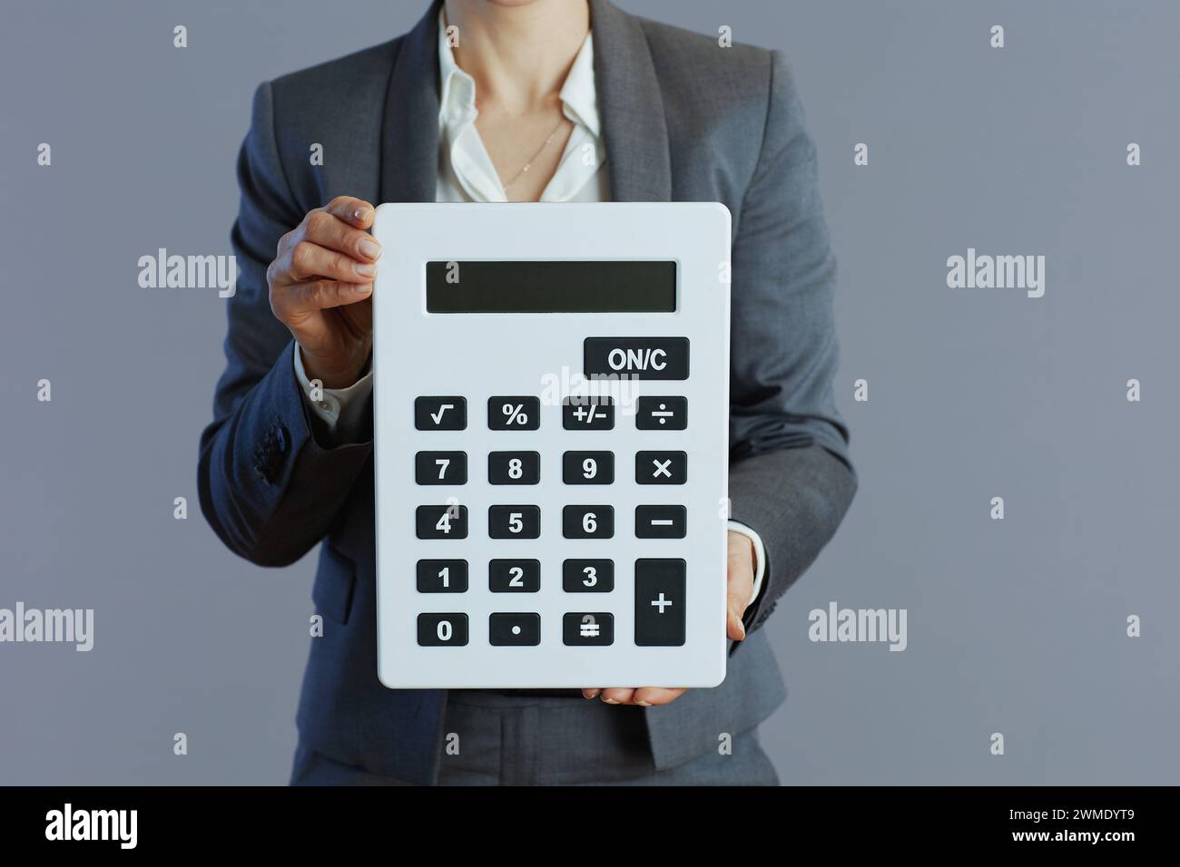 Closeup on woman worker in grey suit with calculator against gray ...