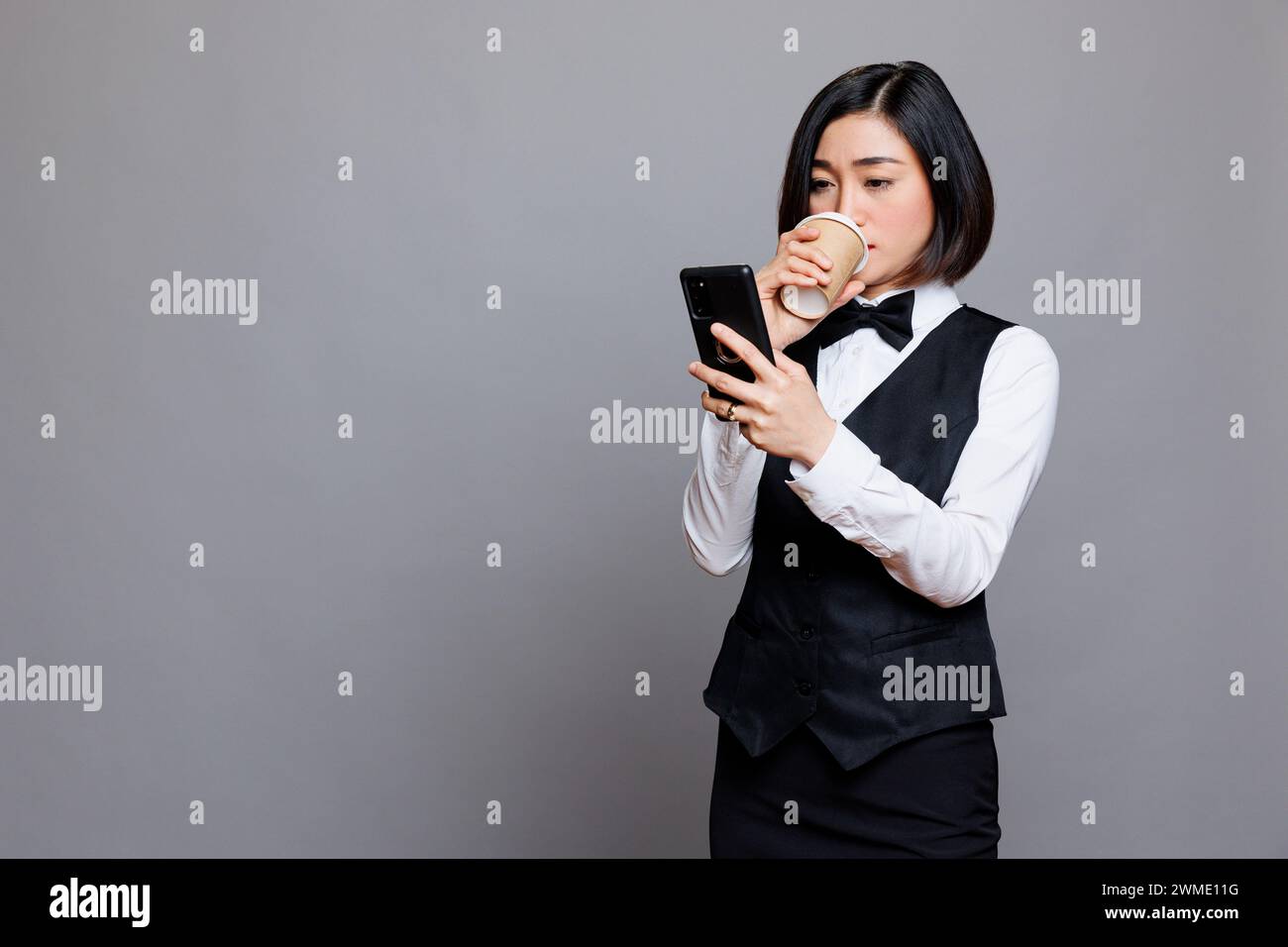Young asian woman wearing waitress uniform tapping on smartphone and ...