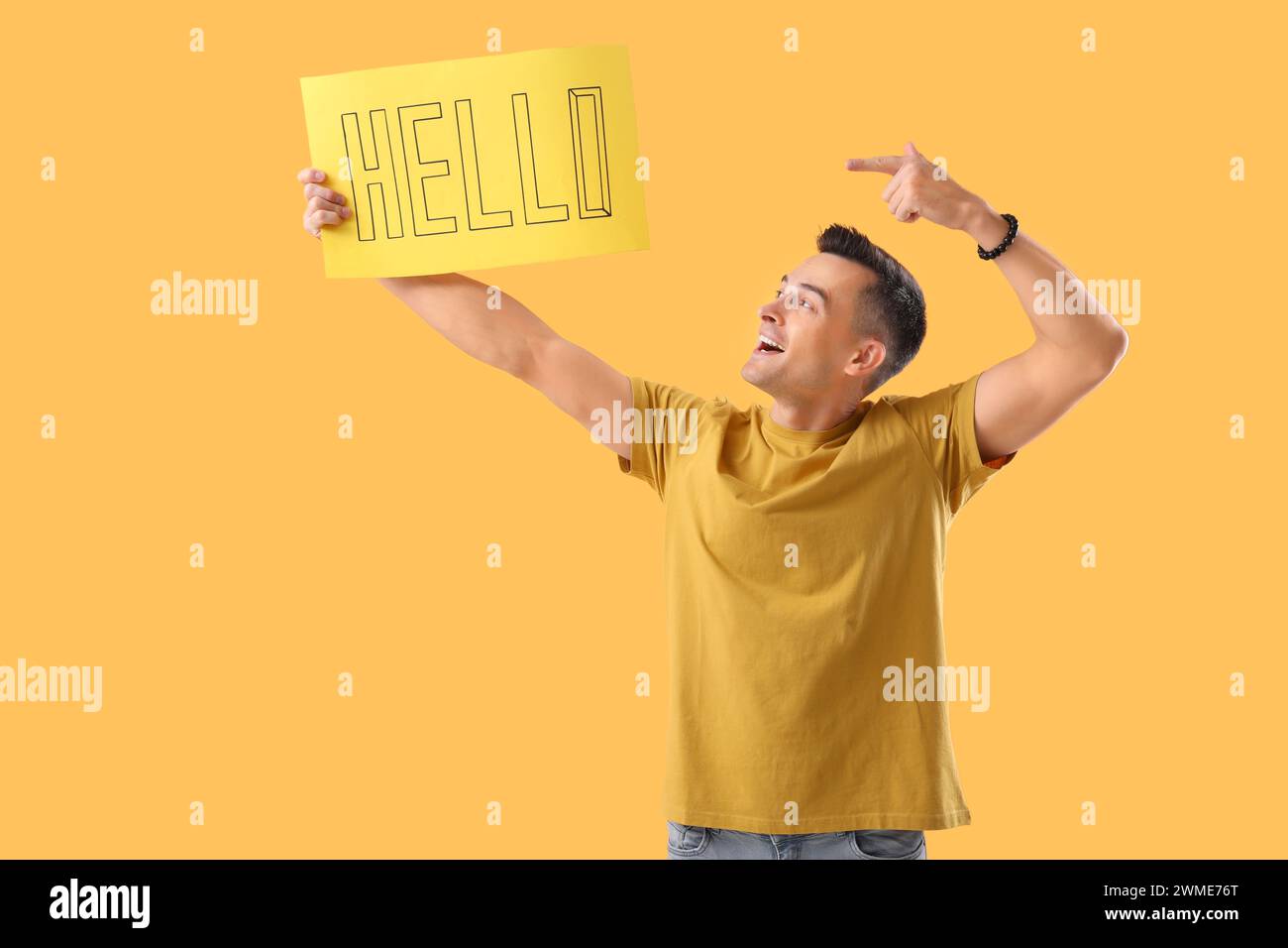 Young man pointing at paper with word HELLO on yellow background Stock ...