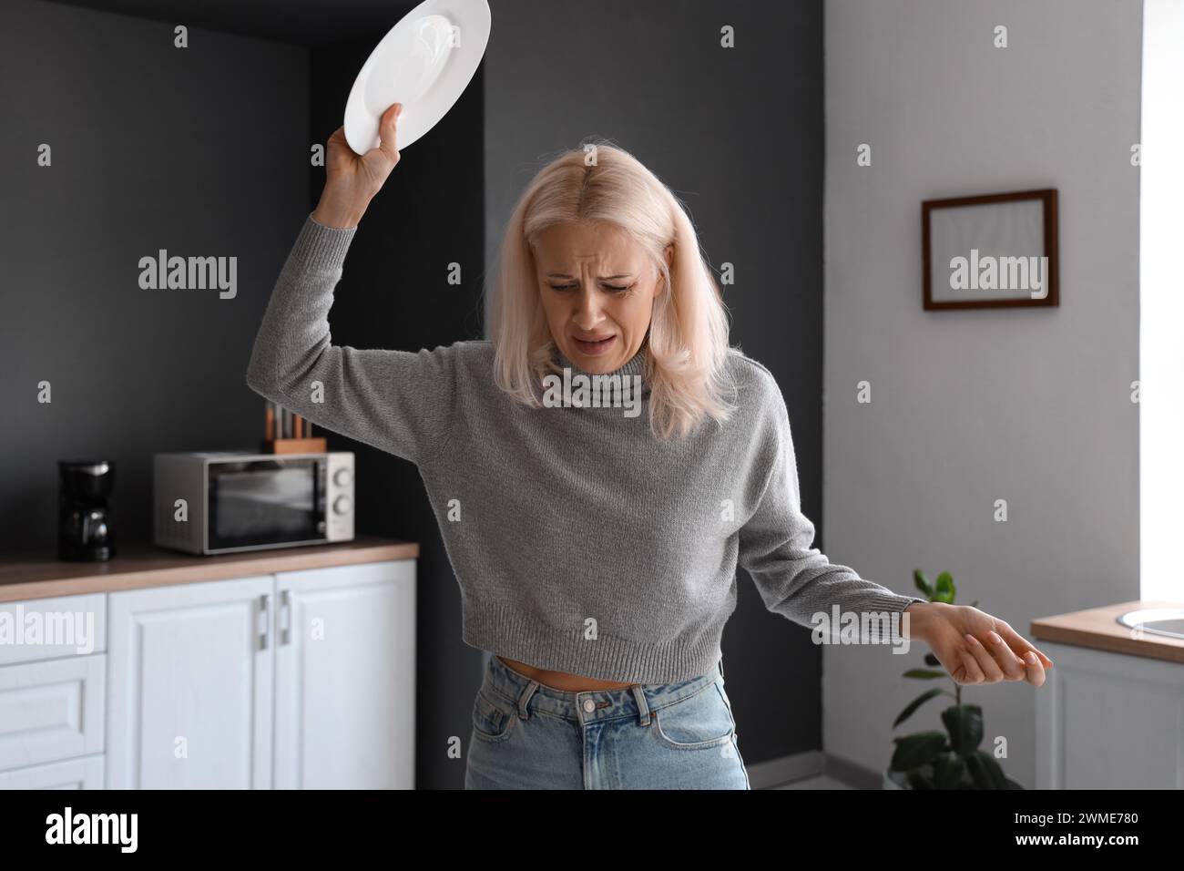 Depressed mature woman smashing plate in kitchen Stock Photo - Alamy