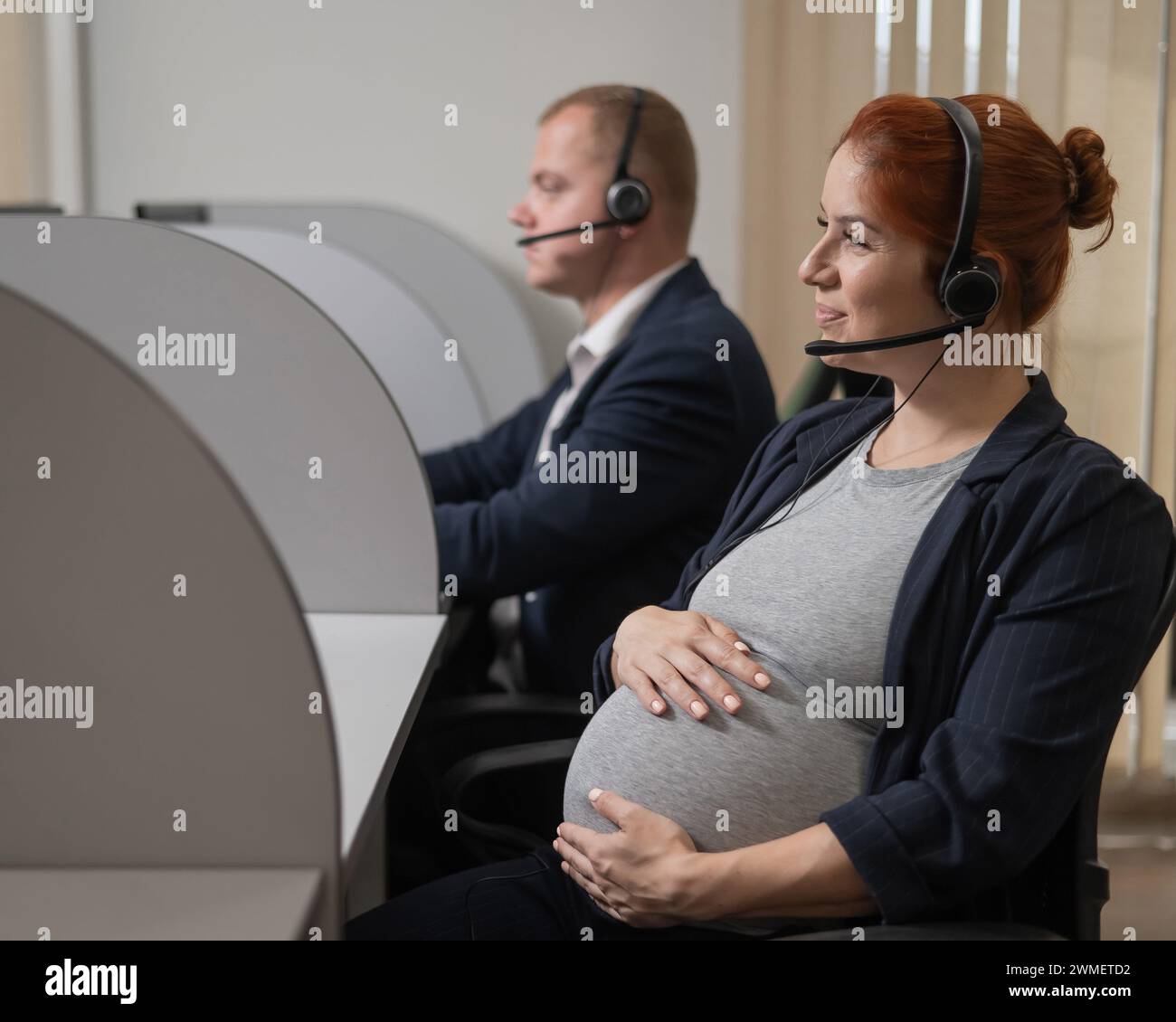 Two friendly call center employees serve customers. Man and pregnant woman talking on a headset ...