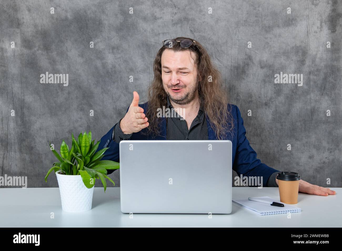 Solemn man with long hair intently focused on his laptop tasks in a ...