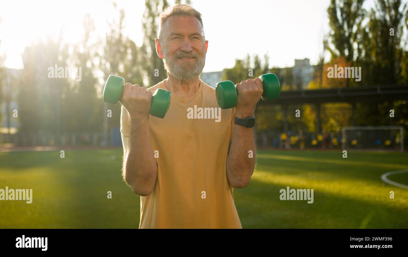 Old Caucasian man grandfather lift dumbbell pump biceps sport athlete ...