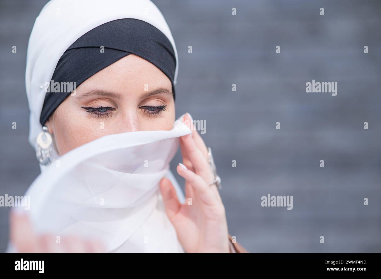 Portrait of a young blue-eyed woman in a hijab against a gray brick ...