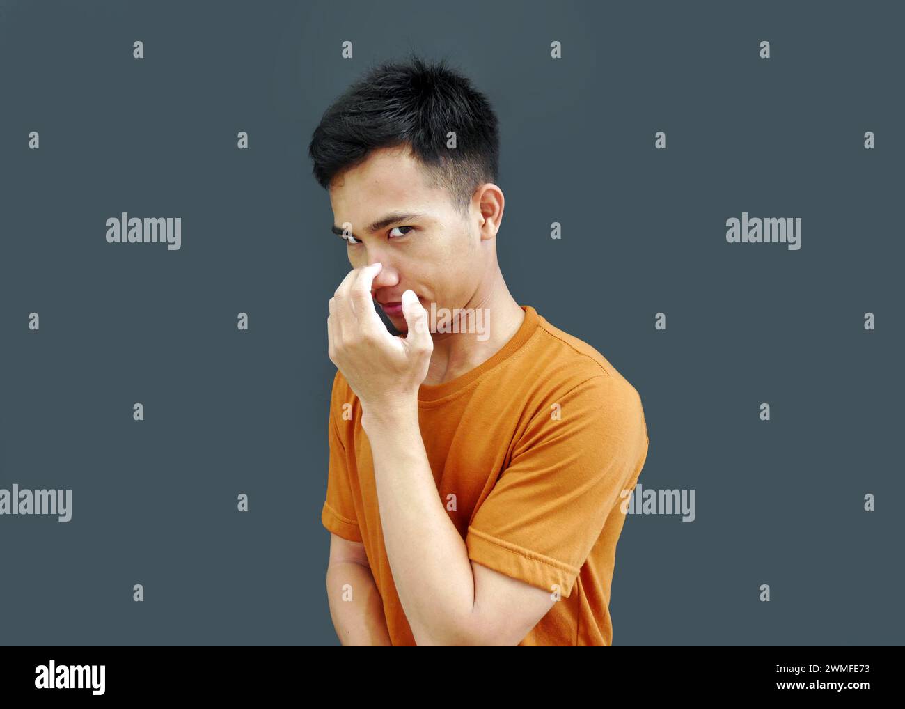 Young Asian man standing aside holding his nose and looking at the ...
