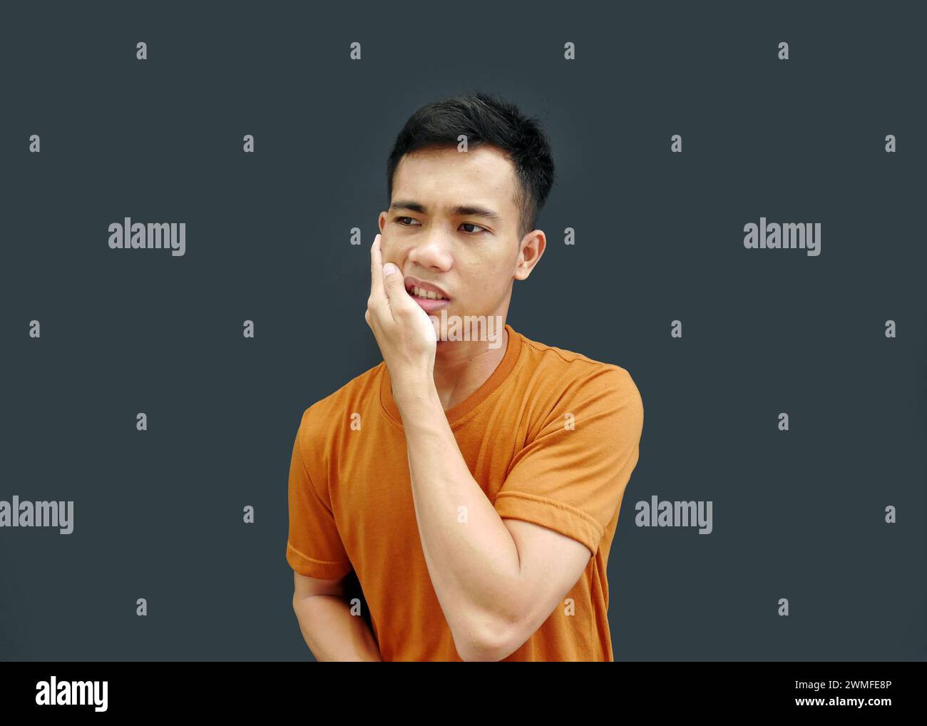 Grimacing young man having severe toothache, holding his cheek with hand, face in pain, isolated ...