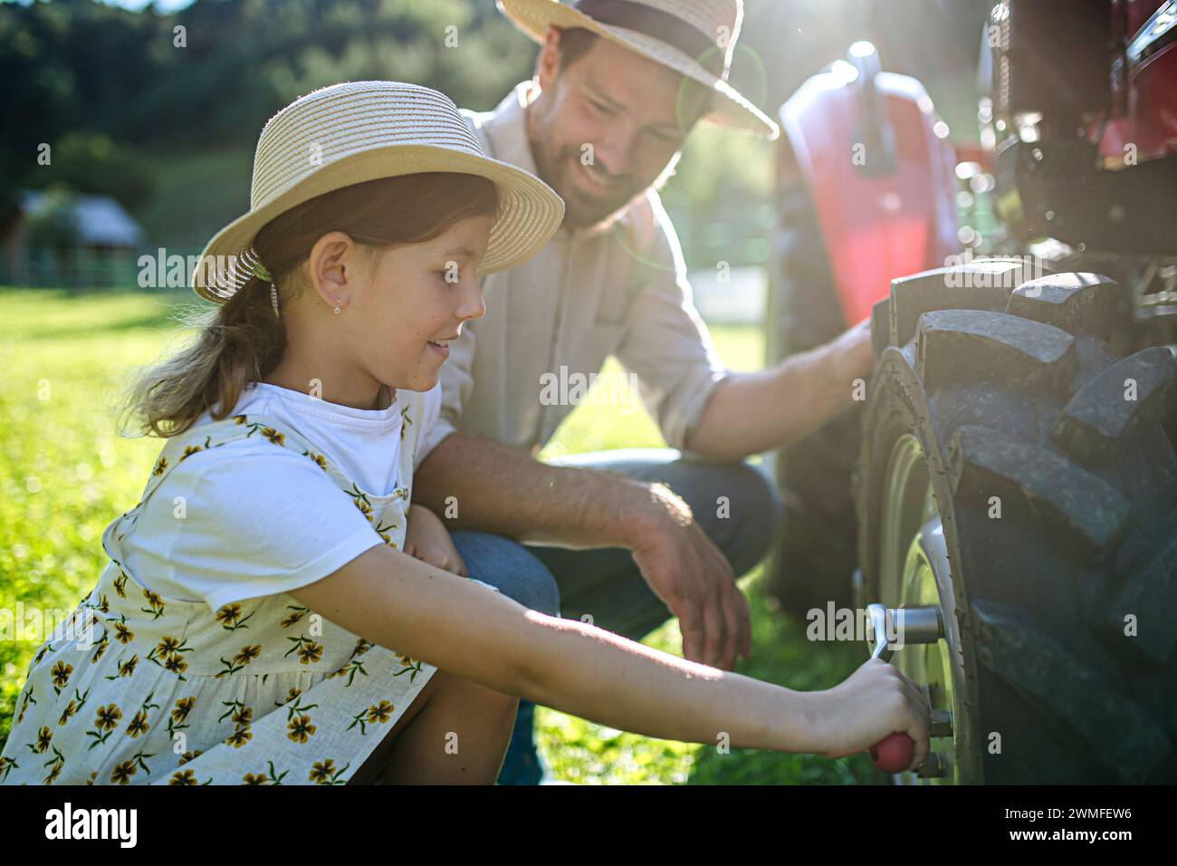 Farmer father teaching daughter how to fix a wheel on a tractor. Young ...