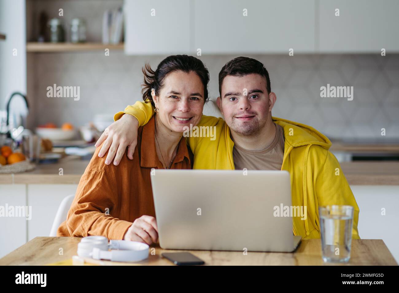 Mom teaching young man with down syndrome, using laptop. Telehealth ...