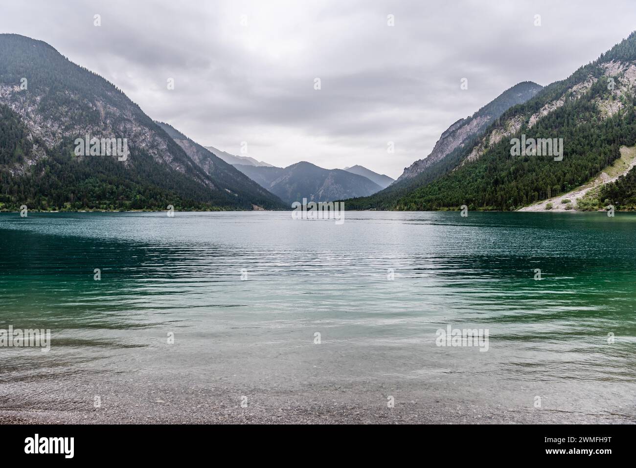 A peaceful lake surrounded by mountains under a cloudy sky, Plansee ...