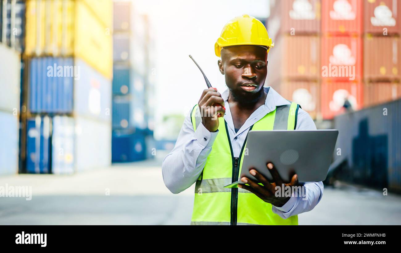 A dock foreman with a laptop and radio standing in front of cargo ...