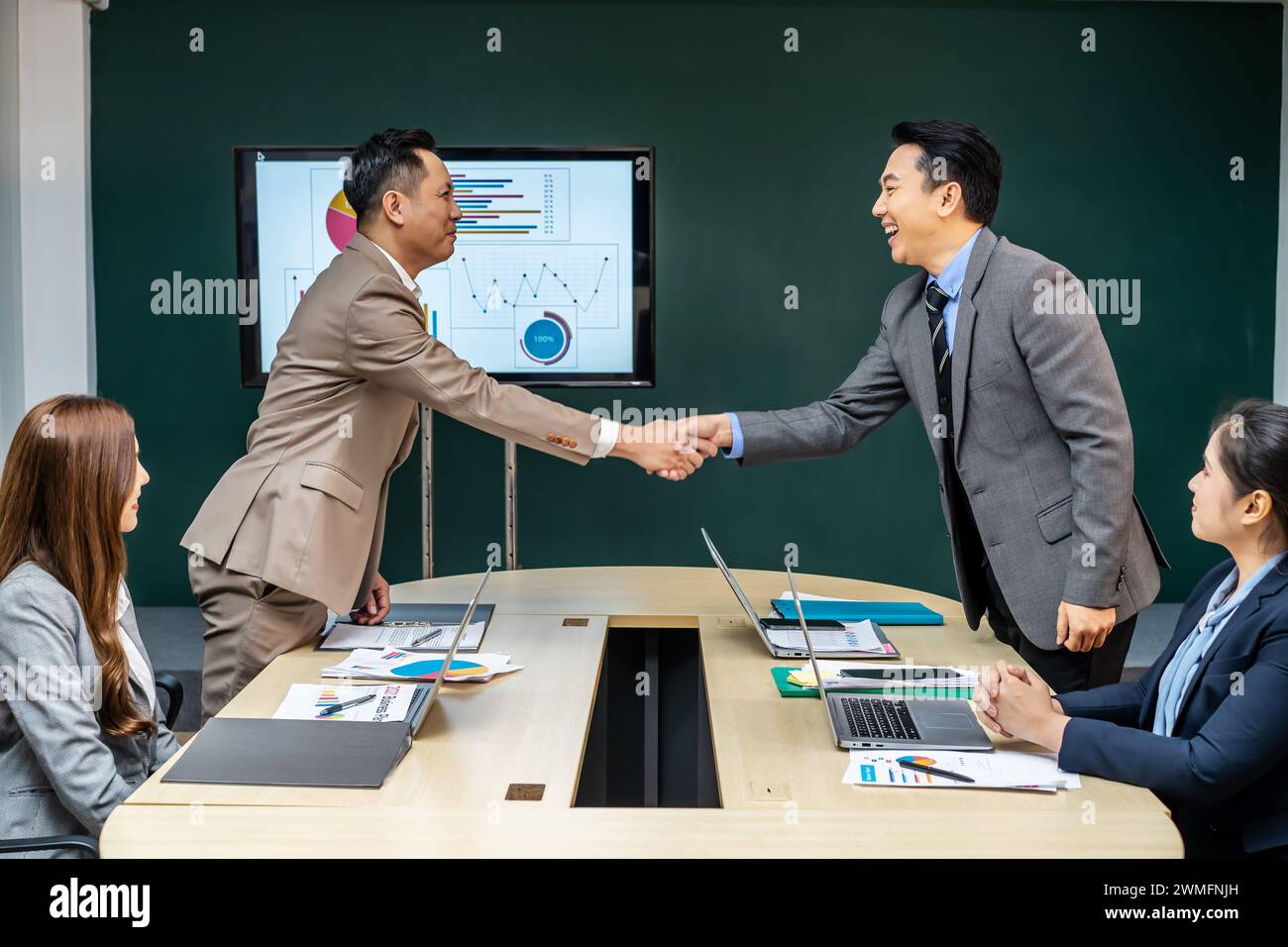 The businessmen shake hands in a meeting room with a projection screen ...