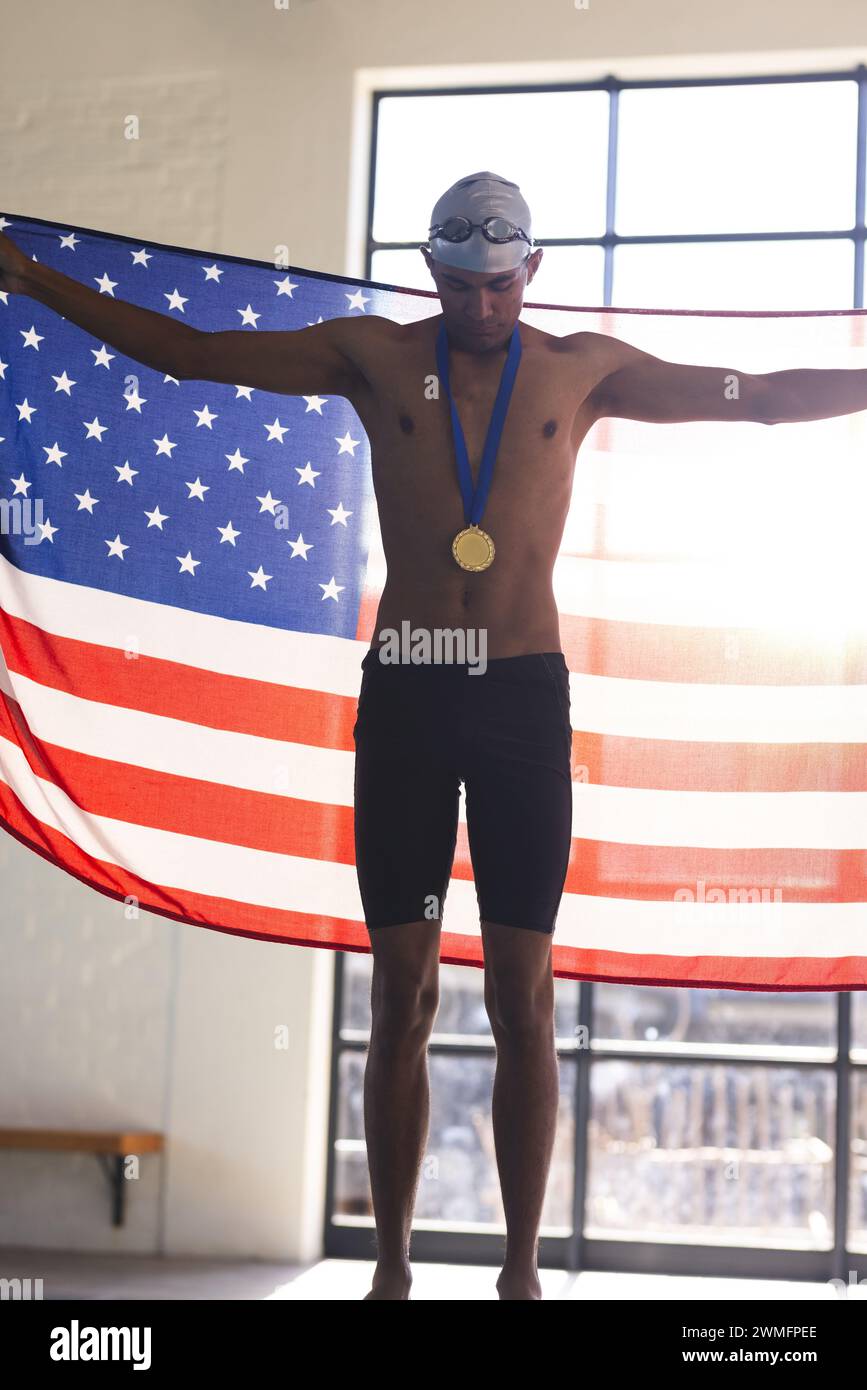 Proud young biracial male athlete swimmer displays a gold medal, with ...