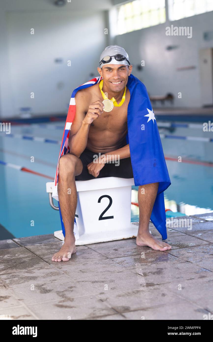 A young biracial male swimmer celebrates at the poolside, draped in an ...