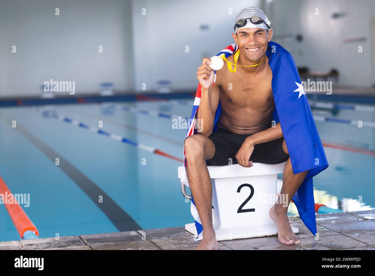 Young biracial male swimmer celebrates at the poolside, draped in an ...