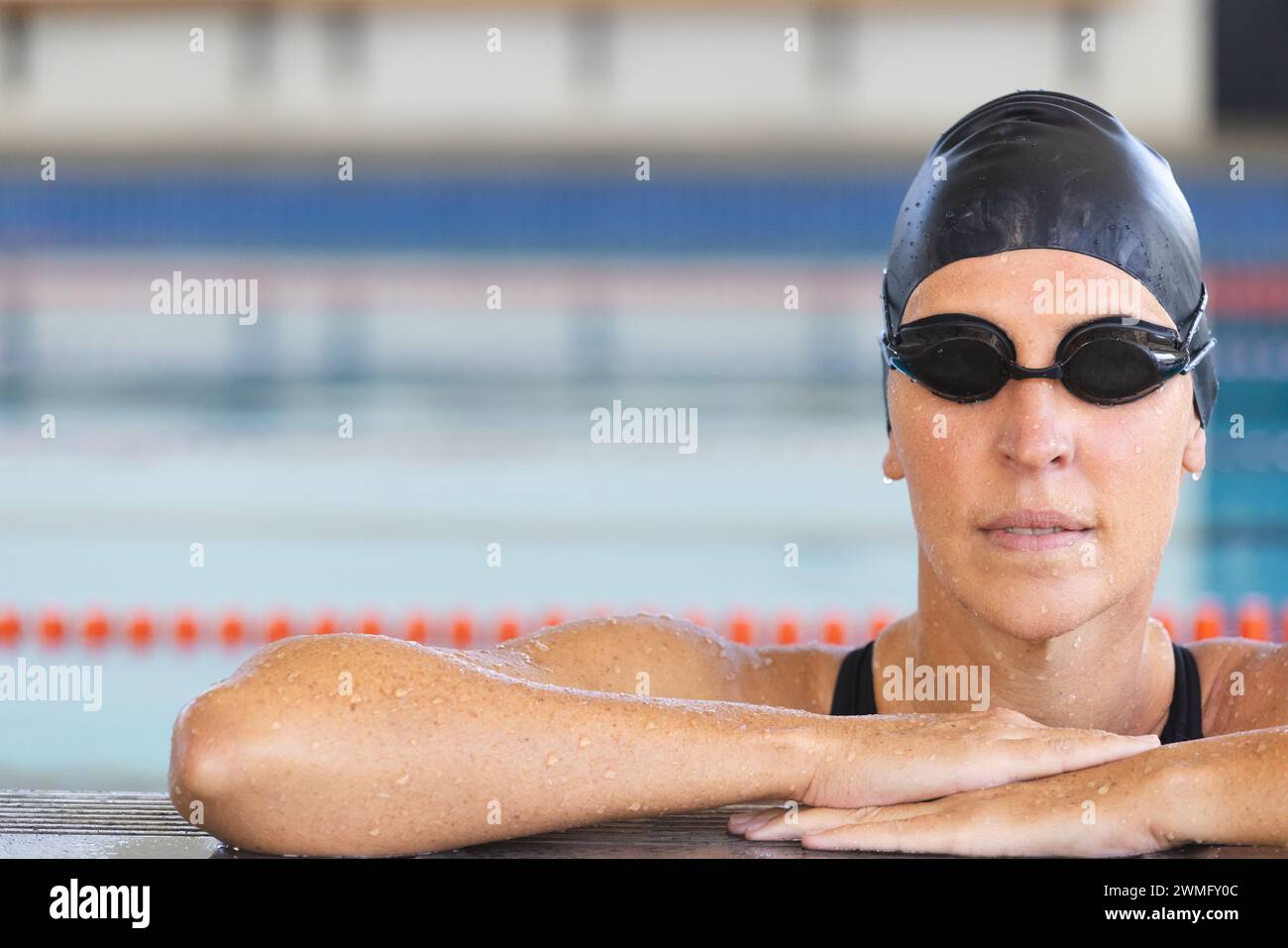 Caucasian female athlete swimmer rests at the pool's edge, with copy ...