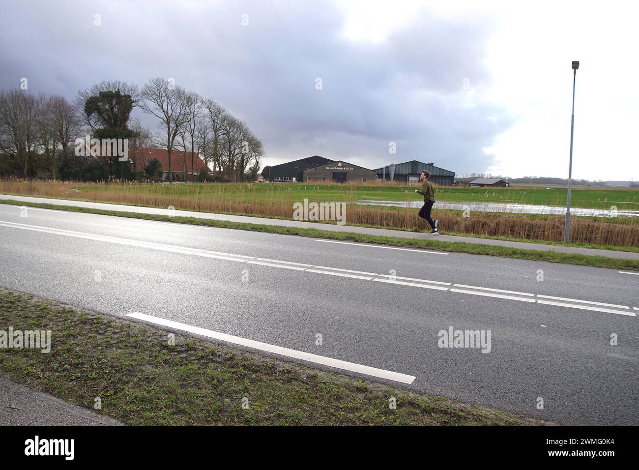 Street, meadows with water from the rain. Very cloudy. Jogger on the ...