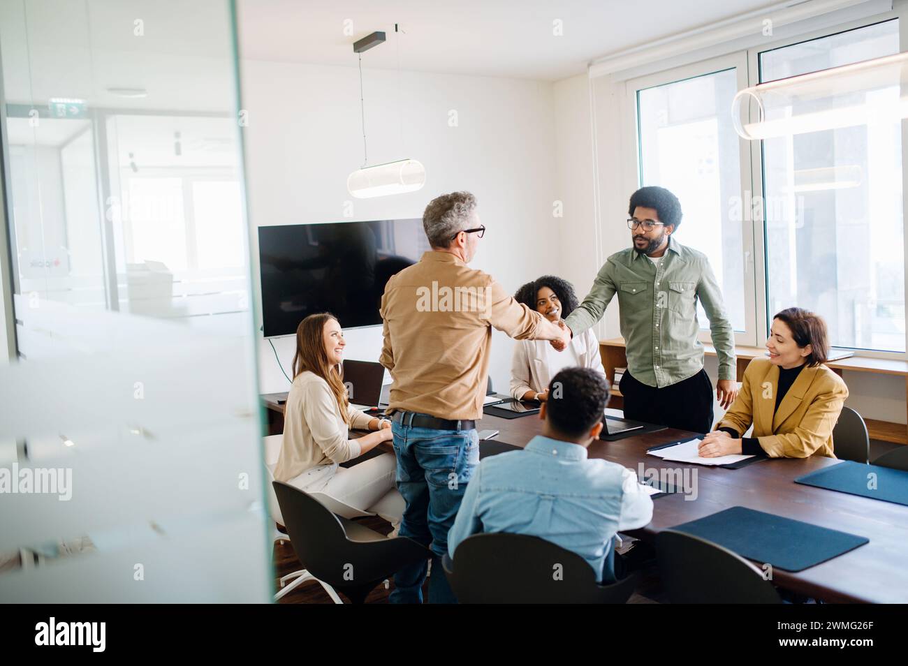 A team circles around a meeting table where a handshake between two ...