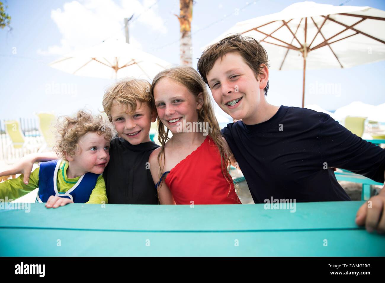 Four Siblings Smile at Camera While Sitting at Turquoise Picnic Table ...