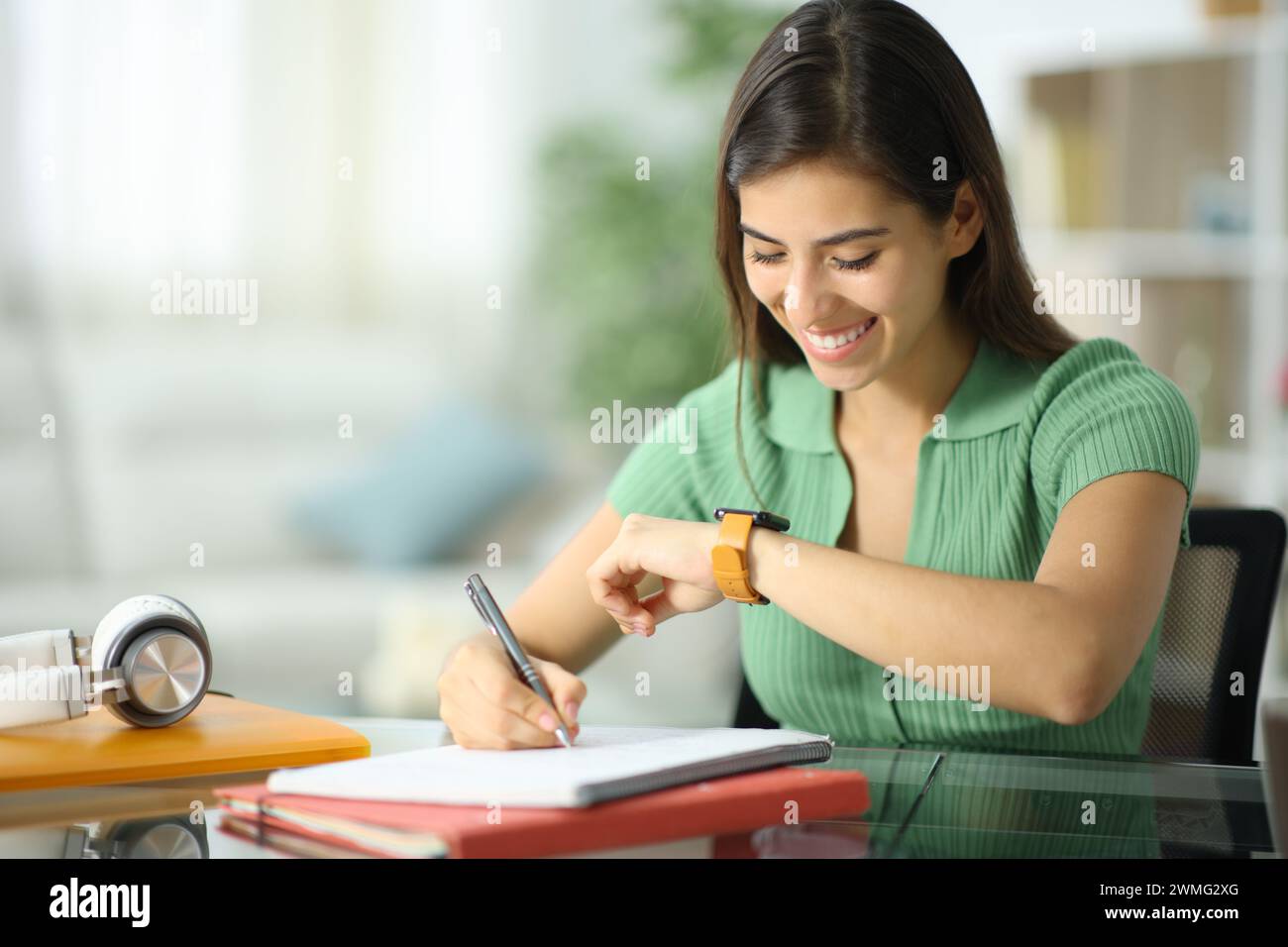 Happy student checking smartwatch taking notes at home Stock Photo - Alamy