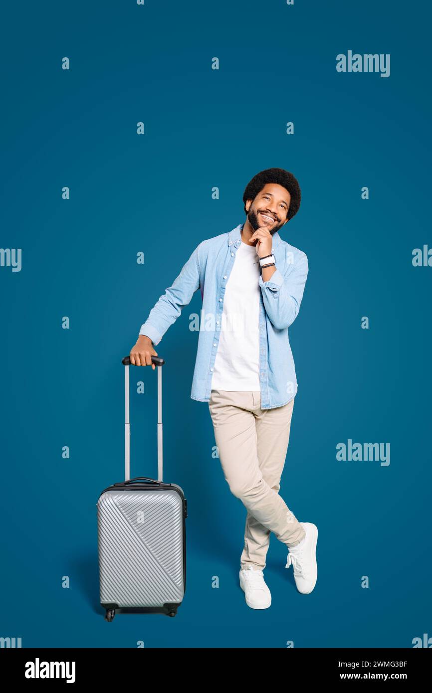 A young Brazilian man standing with suitcase in a thoughtful pose ...