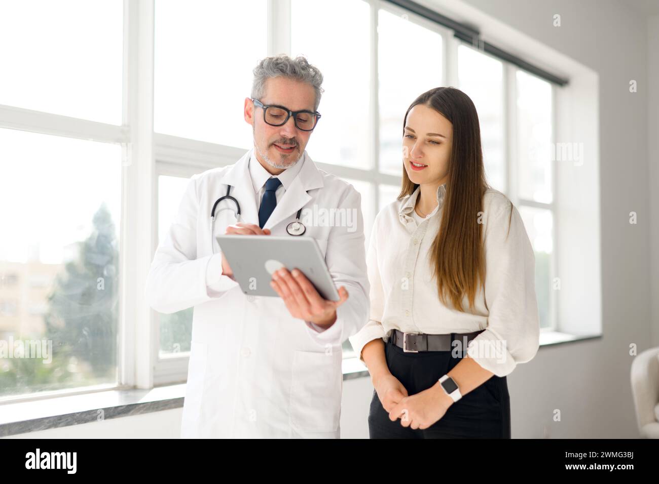 In this image, a mature doctor with a digital tablet discusses ...