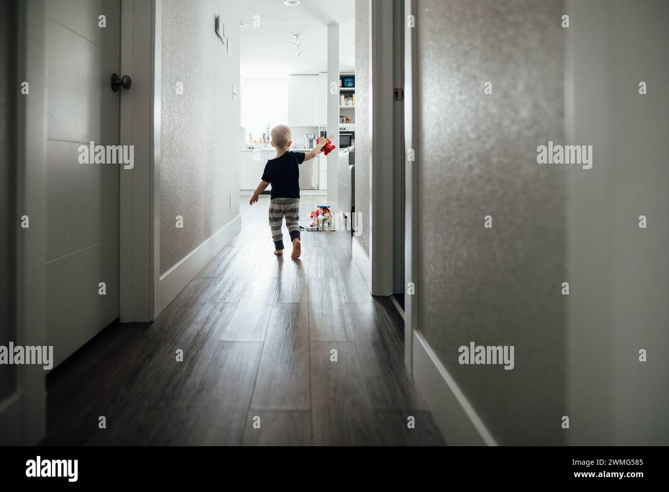 Rear view of small boy walking down hallway pretending to fly plane ...