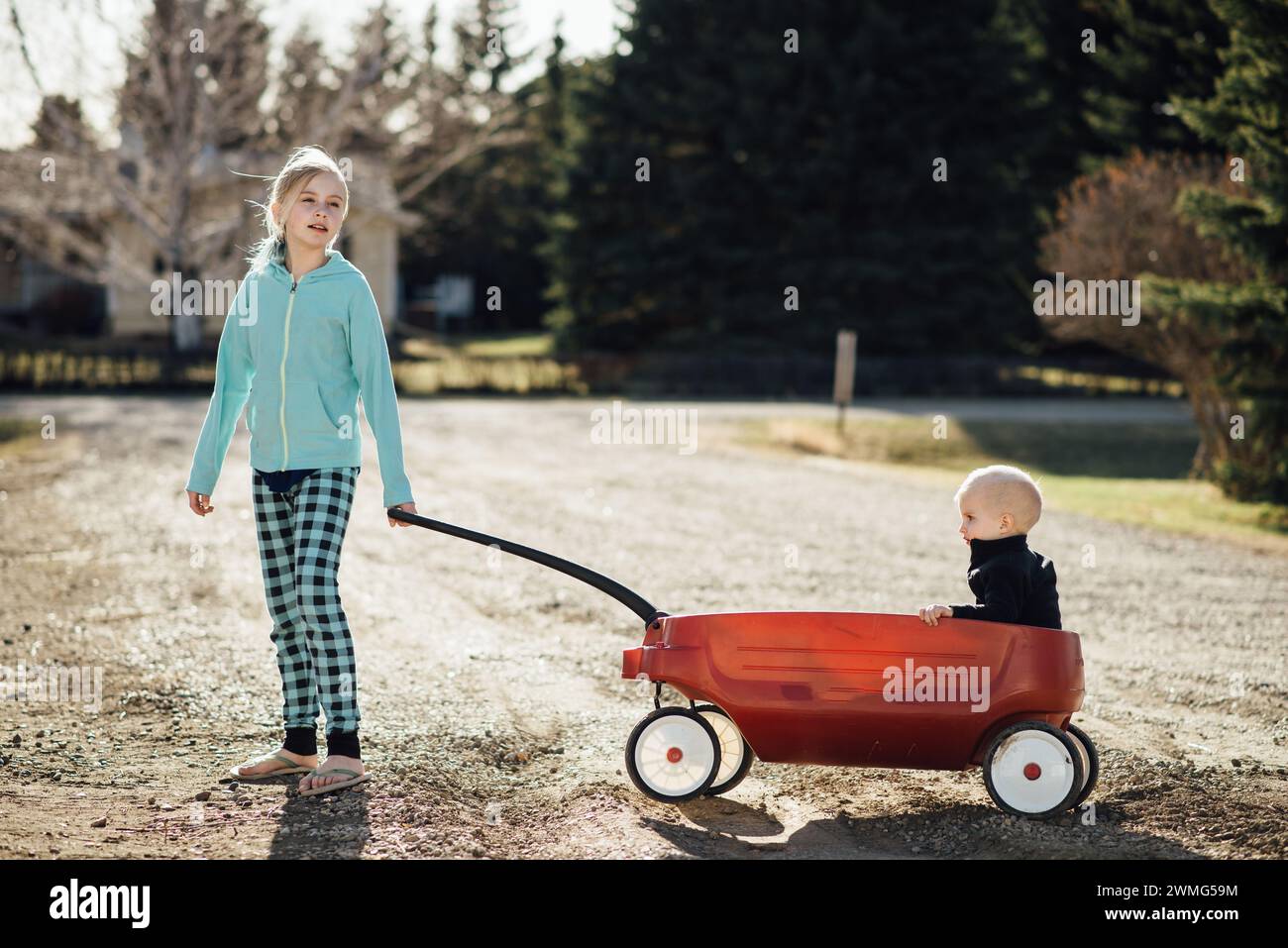 Full view of preteen girl pulling boy in toy wagon Stock Photo - Alamy