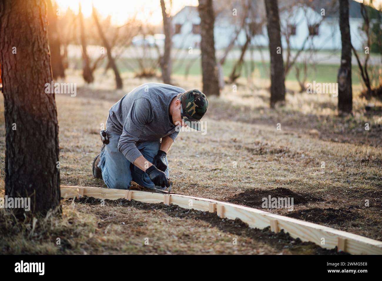 Wide front view of man kneeling while doing manual labor in yard Stock ...