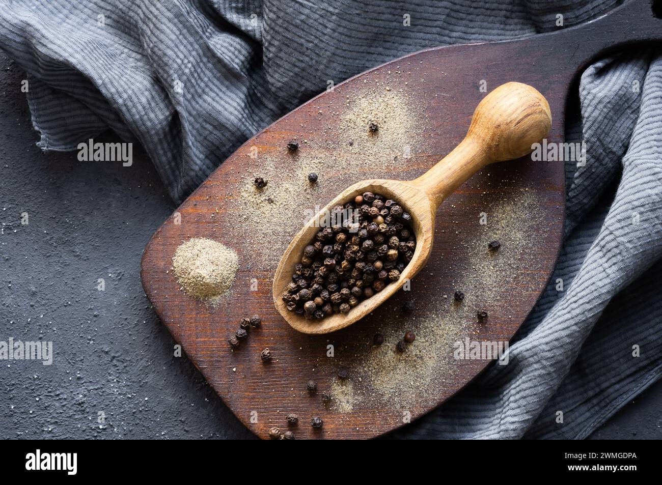 Heap of black pepper, peppercorns in spoon with milled powder on rustic ...