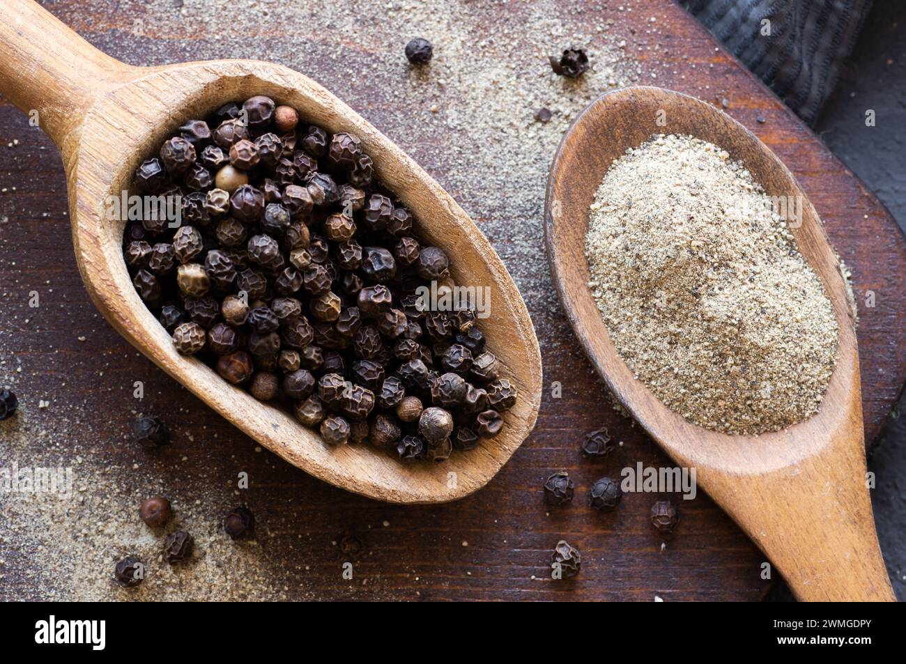 Heap of black pepper, peppercorns in spoon with milled powder on rustic ...