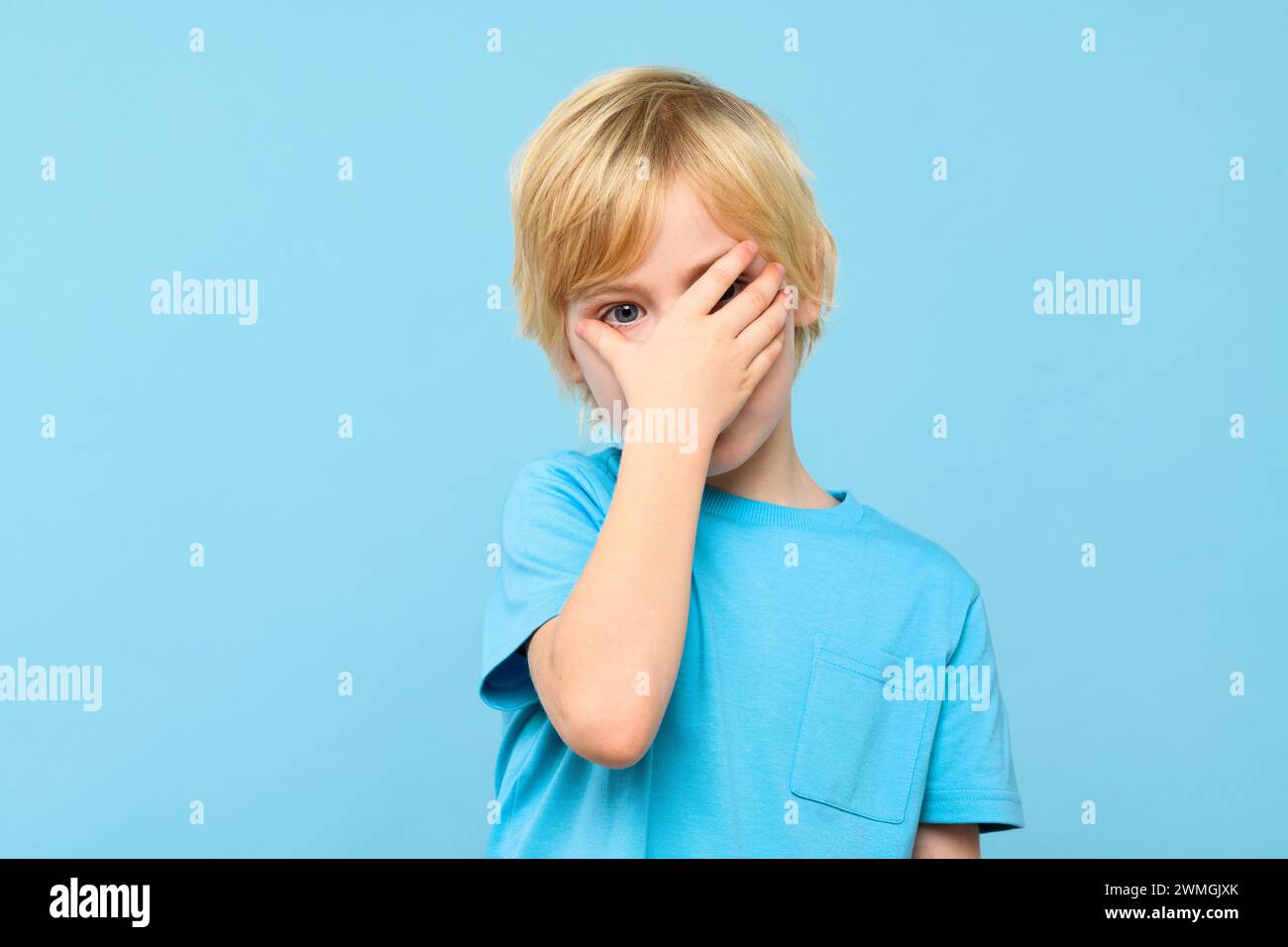 Emotional young boy covering face with hands isolated over pastel blue ...