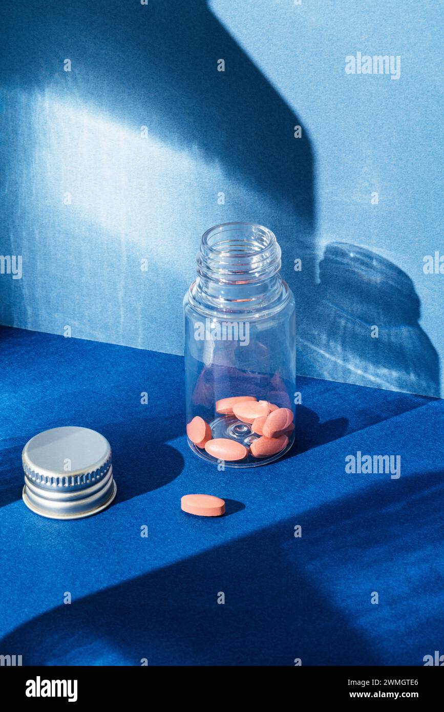 Pink tablet pills in glass bottle on blue background with light and ...