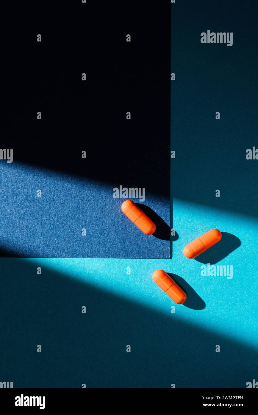 Orange capsule pills on blue background with copy space. Partial light ...
